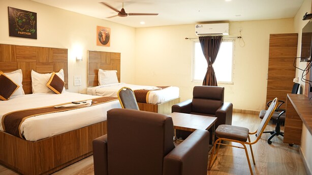 Quarto de hotel com duas camas, uma escrivaninha, uma cadeira, uma TV e um ventilador de teto.