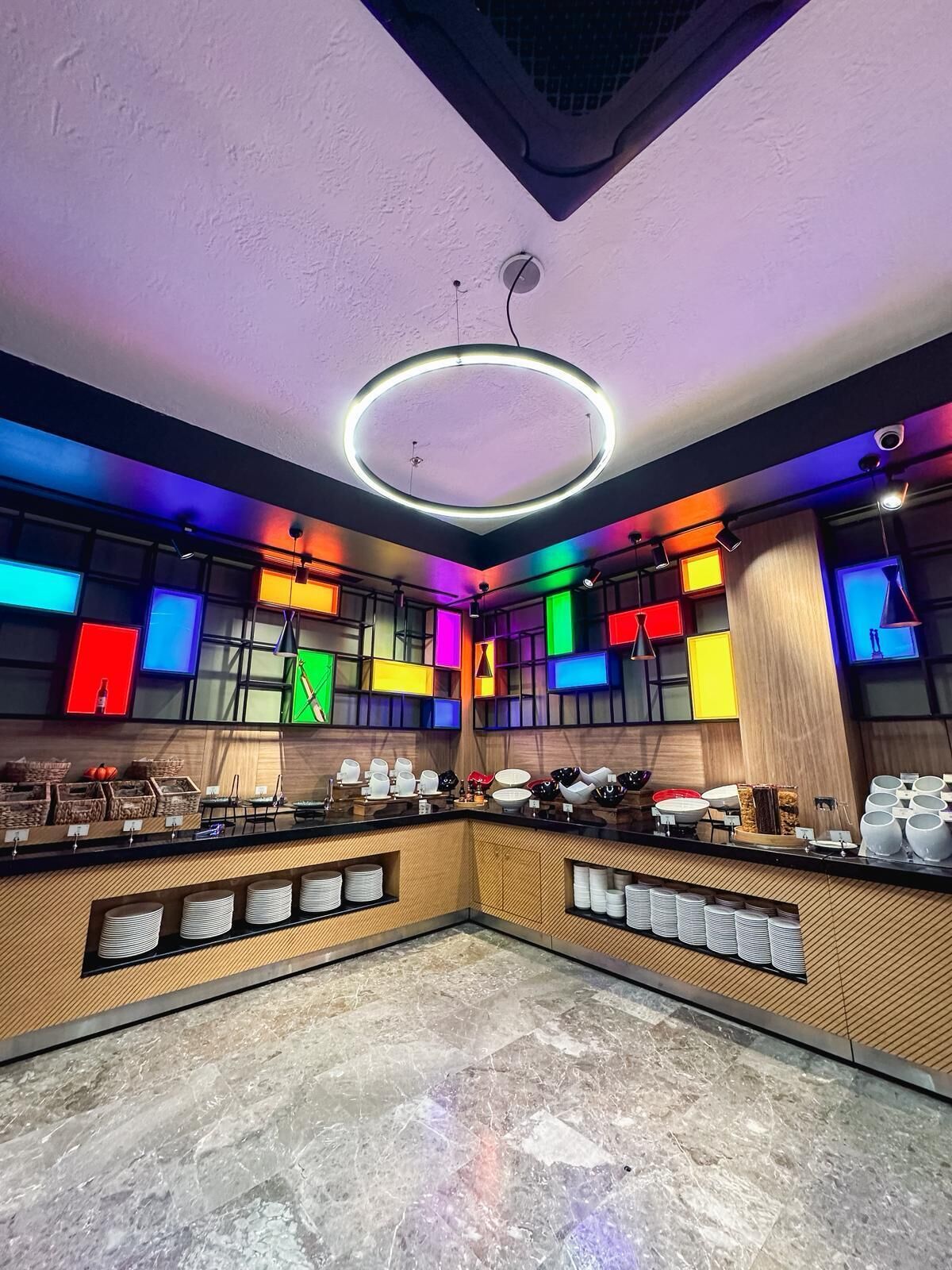 Um interior moderno com uma luminária circular central, um balcão de buffet com diversos pratos e um piso estampado.
