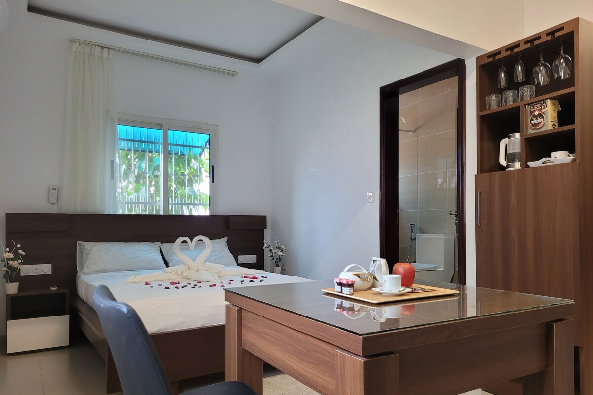 Quarto de hotel com cama, mesa de cabeceira e escrivaninha com cadeira.