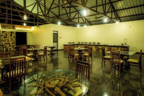 Um espaço amplo e interno com várias mesas e cadeiras para refeições, uma lareira de pedra e um teto alto com vigas de metal.