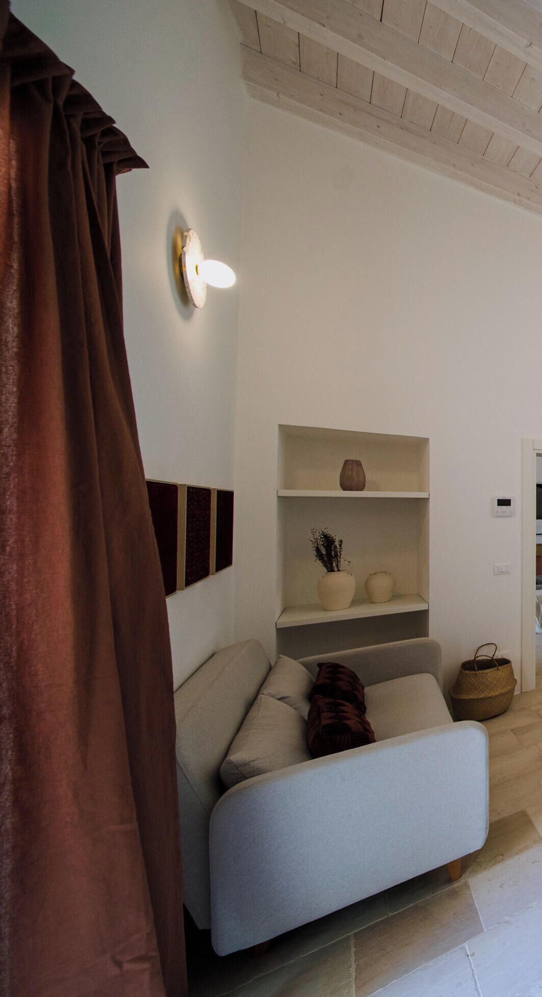 Uma sala de estar moderna com sofá, luminária fixada na parede e uma prateleira com objetos decorativos.