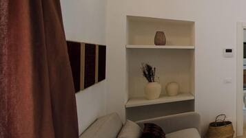 Uma sala de estar moderna com sofá, luminária fixada na parede e uma prateleira com objetos decorativos.