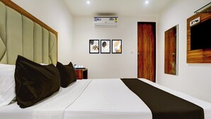 Quarto de hotel com cama, mesa de cabeceira com chávenas e chaleira, ar condicionado fixado na parede e obras de arte emolduradas.