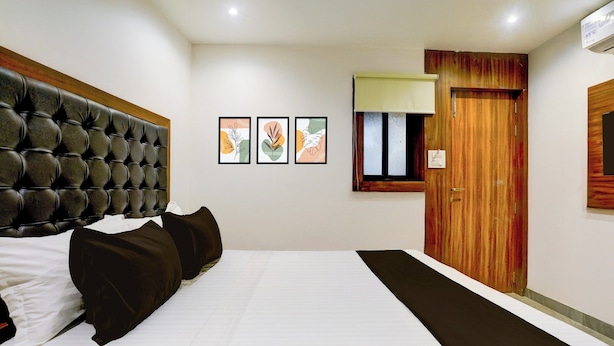 Quarto de hotel com uma cama grande, cabeceira, porta de madeira e três obras de arte emolduradas na parede.
