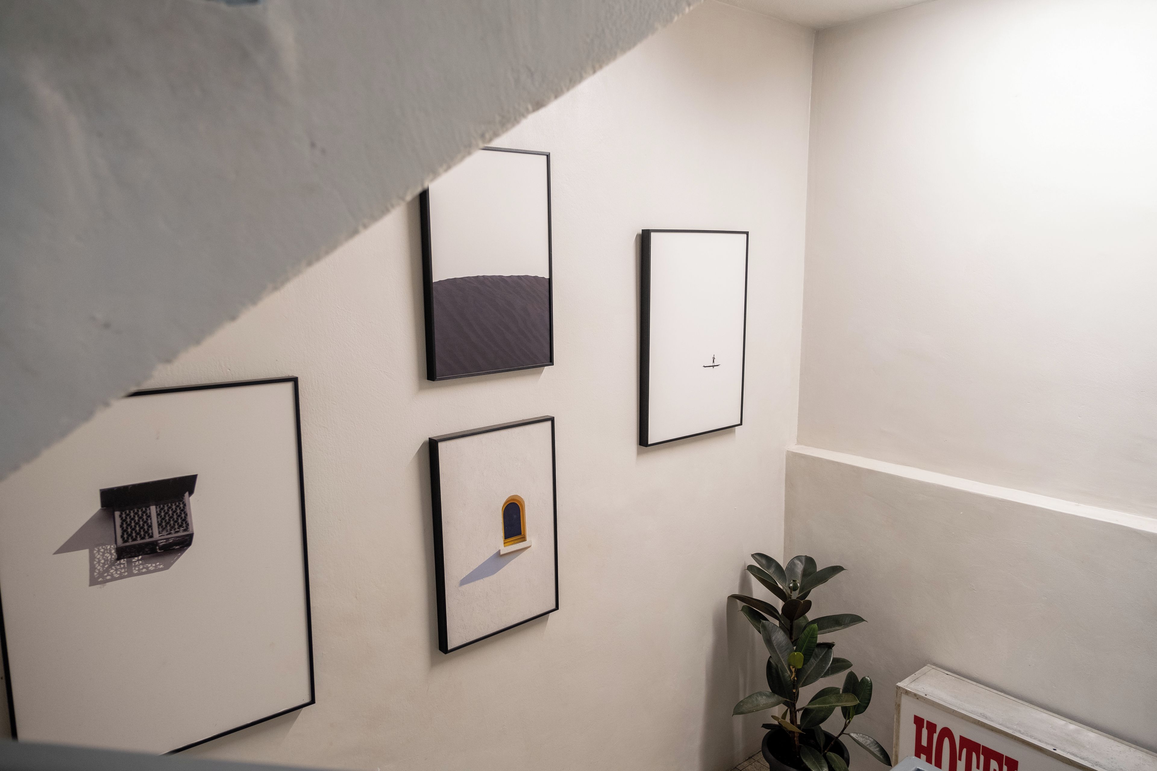 Paredes com quatro quadros, um vaso de planta e uma placa com a palavra 'HOTEL' à direita.