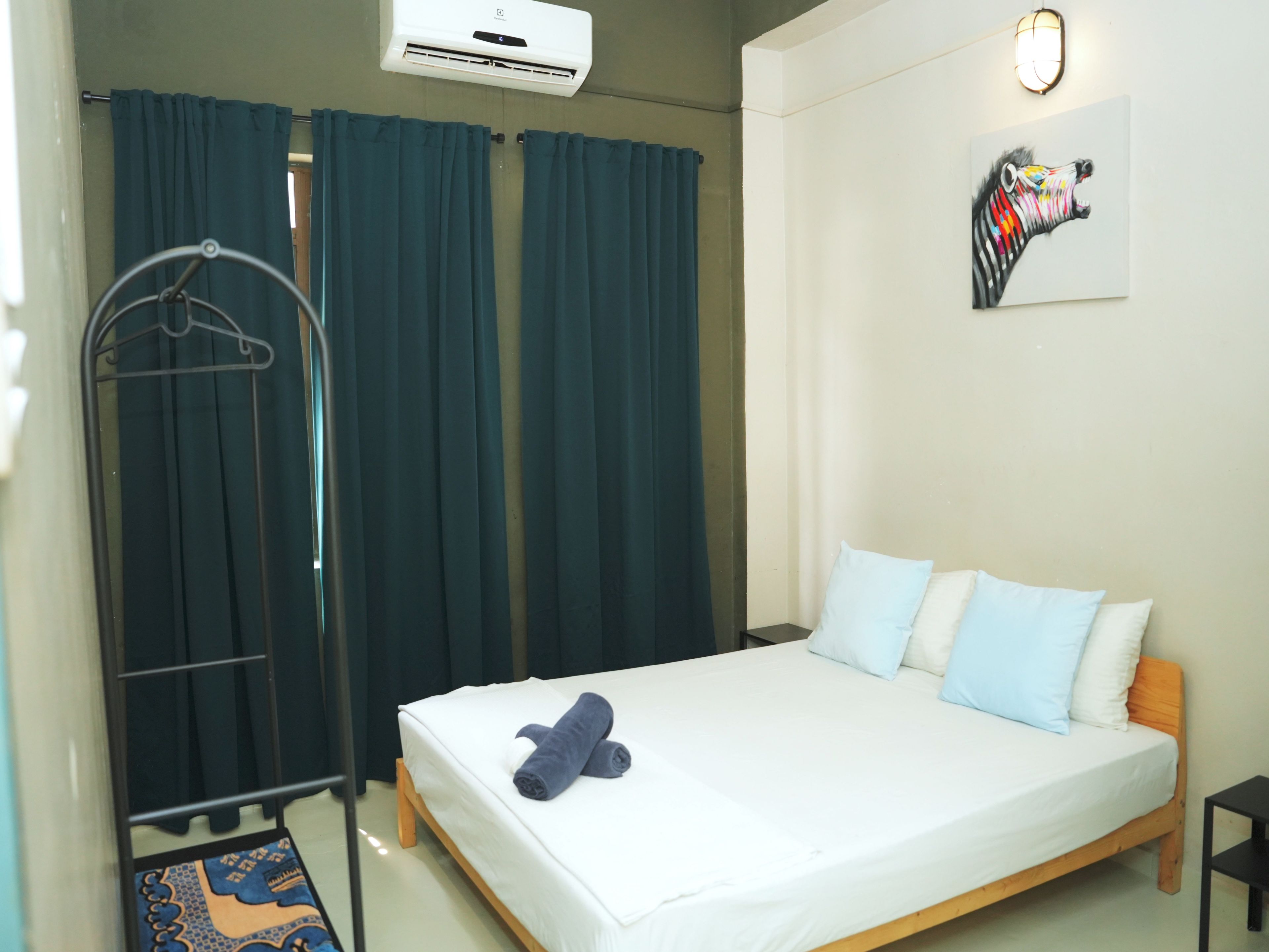 Quarto com cama, porta-toalhas suspenso e ar-condicionado fixado na parede.