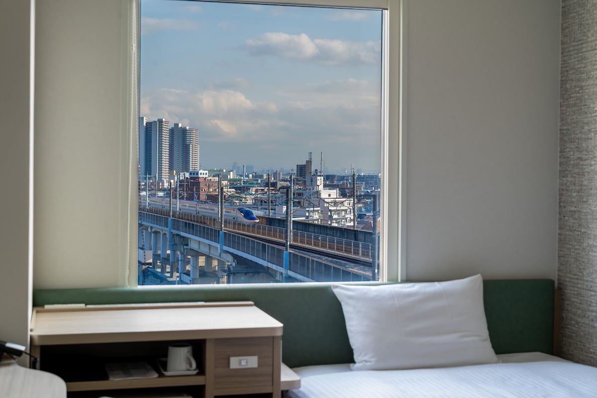 Quarto de hotel com uma grande janela que oferece vista para a paisagem urbana, incluindo uma ponte e arranha-céus.
