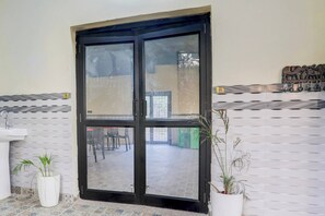 Um quarto com piso de azulejos, porta de vidro com moldura preta, pia branca e duas plantas em vasos.