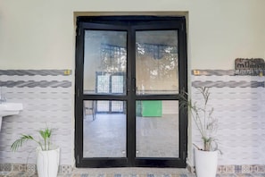 Entrada de hotel com porta preta, paredes azulejadas e plantas em vasos.