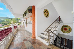 Um corredor com piso xadrez, escada com corrimãos de metal e detalhes decorativos nas paredes.
