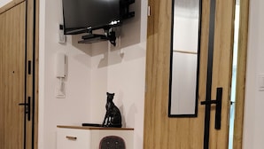 Quarto moderno com televisão de tela plana na parede, guarda-roupa de madeira, penteadeira branca, um par de chinelos e uma mesa redonda com duas cadeiras.