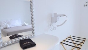 Quarto de hotel com cama, espelho com contas de pérola, porta-toalhas e secador de cabelo fixado na parede.