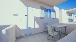 Uma varanda com mesa e cadeiras, uma porta e uma janela com persianas.