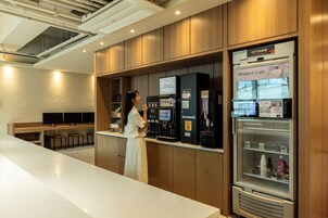 Um hall de hotel moderno com um balcão de recepção extenso, placa de circuito fechado de TV e um refrigerador de cafeteria com sobremesas.