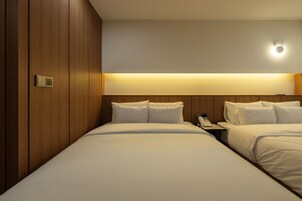 Quarto de hotel com duas camas, uma mesinha de cabeceira com telefone e uma luminária fixada na parede.