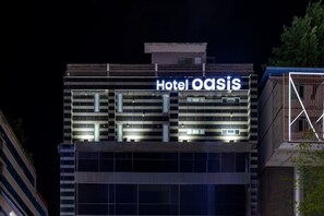 Um edifício de hotel moderno com uma placa grande exibindo 'Hotel Oasis' à noite.