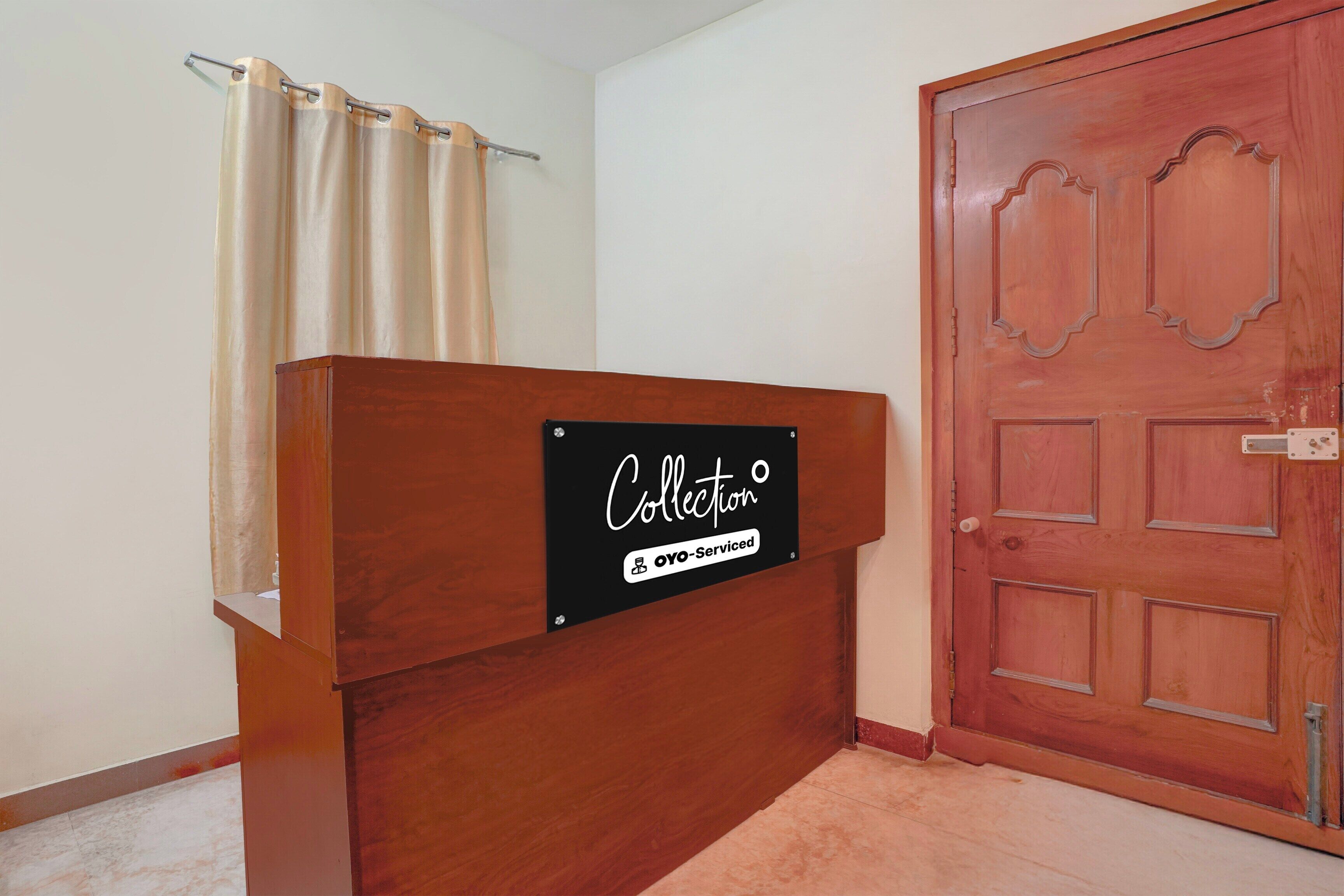 Uma mesa de madeira com uma placa que diz 'Collection' e 'Oyo-Serviced' em um quarto com porta de madeira e cortina.
