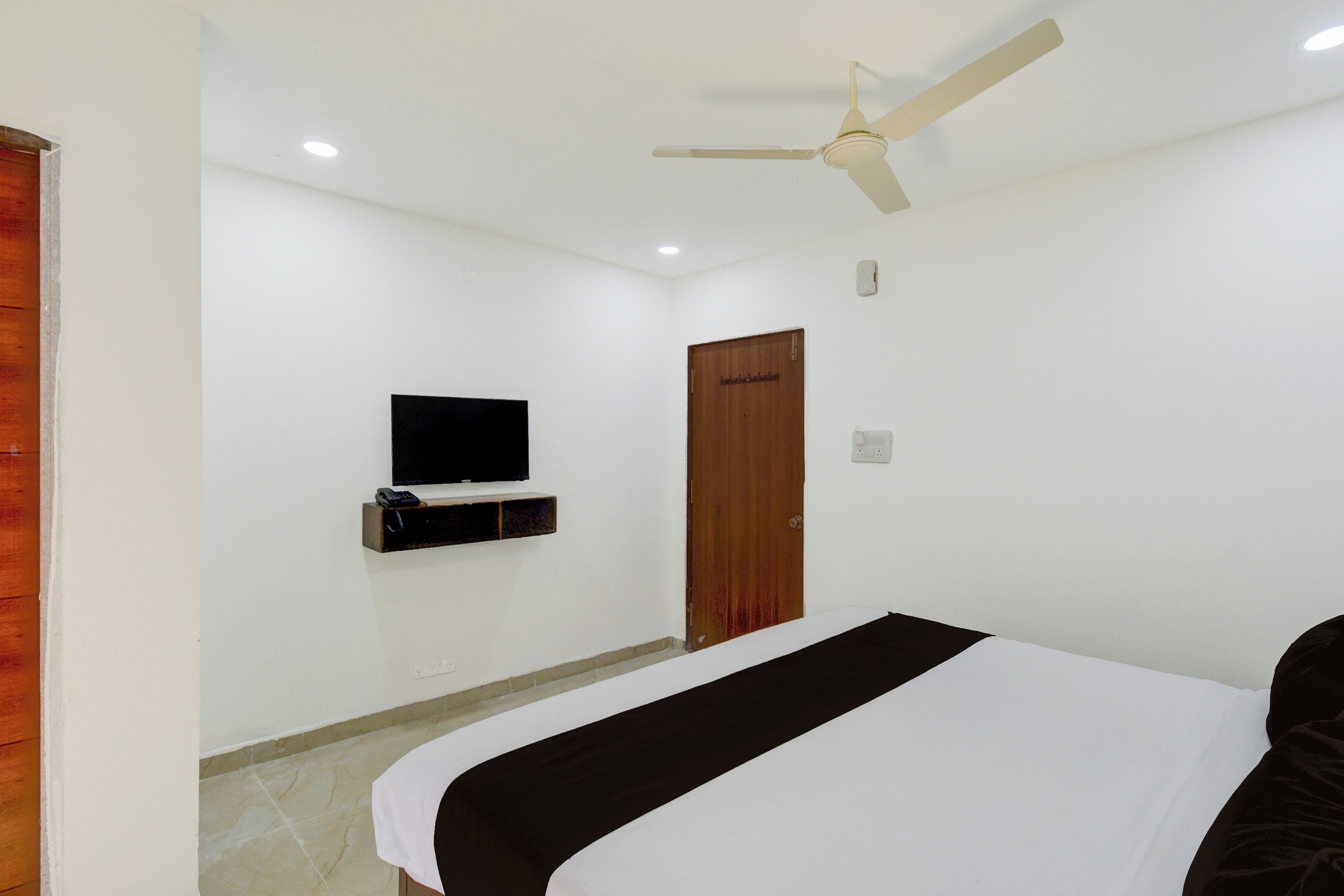 A bedroom with a bed, a ceiling fan, a mounted TV, and a wooden door.