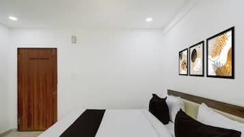 Quarto de hotel com porta de madeira, cama com roupa de cama branca e preta, e três quadros decorativos na parede.