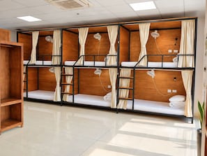 Quarto em dormitório com beliches, cabeceiras de madeira e ventiladores de teto.