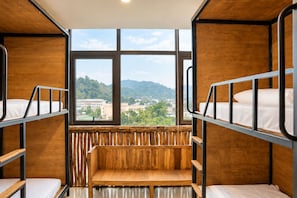 Quarto com beliche e vista para a paisagem urbana através de amplas janelas.
