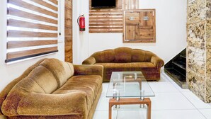 Uma sala de estar com dois sofás, uma mesa de centro de vidro, painéis de madeira, uma televisão na parede e uma lareira.