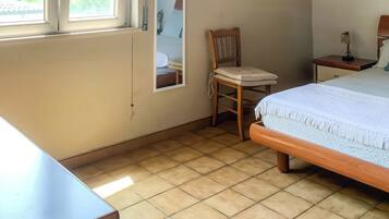 Quarto com teto de madeira, uma cama, uma cadeira, mesa de cabeceira, luminária, janela e espelho.