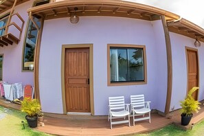 Um edifício com porta de madeira, uma janela e duas cadeiras brancas em um deck de madeira.