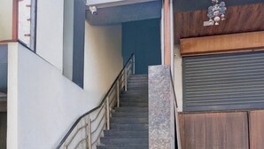 Escada que leva a uma porta de madeira com uma persiana de metal, uma câmera de segurança acima e um elemento decorativo sobre a porta.