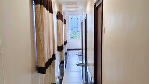 Um corredor de hotel com piso de mármore, uma porta à direita e uma janela no final.