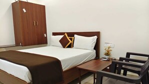 Quarto de hotel com uma cama, um guarda-roupa de madeira, uma mesa de cabeceira com um vaso e uma cadeira.