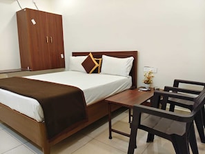 Quarto de hotel com uma cama, um guarda-roupa de madeira, uma mesa de cabeceira com um vaso e uma cadeira.