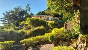 Uma casa numa encosta com muro de pedra e vegetação exuberante.