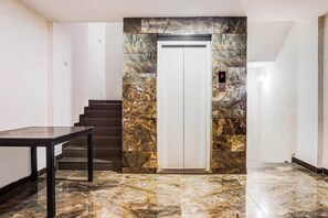 Um corredor com piso de mármore, escada e porta com mostrador digital de elevador.