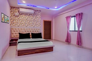 Quarto com cama, ar-condicionado na parede, papel de parede estampado, porta e janela com cortinas.