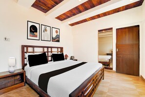 Quarto com estrutura de cama de madeira, mesa de cabeceira e luminária na parede. Há uma porta que dá para outro cômodo.