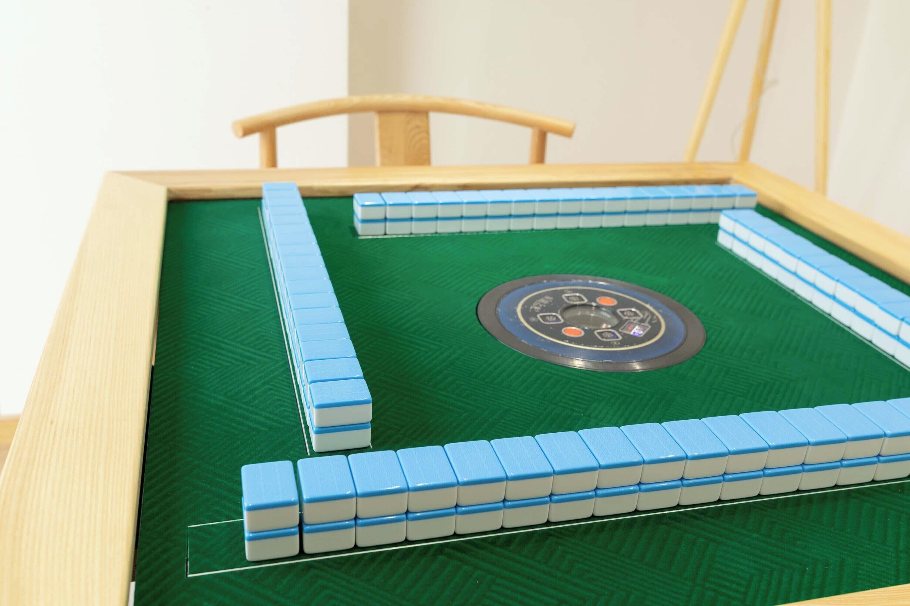Uma mesa verde coberta de feltro, com estrutura de madeira, um girador circular e peças de jogo azuis e brancas.
