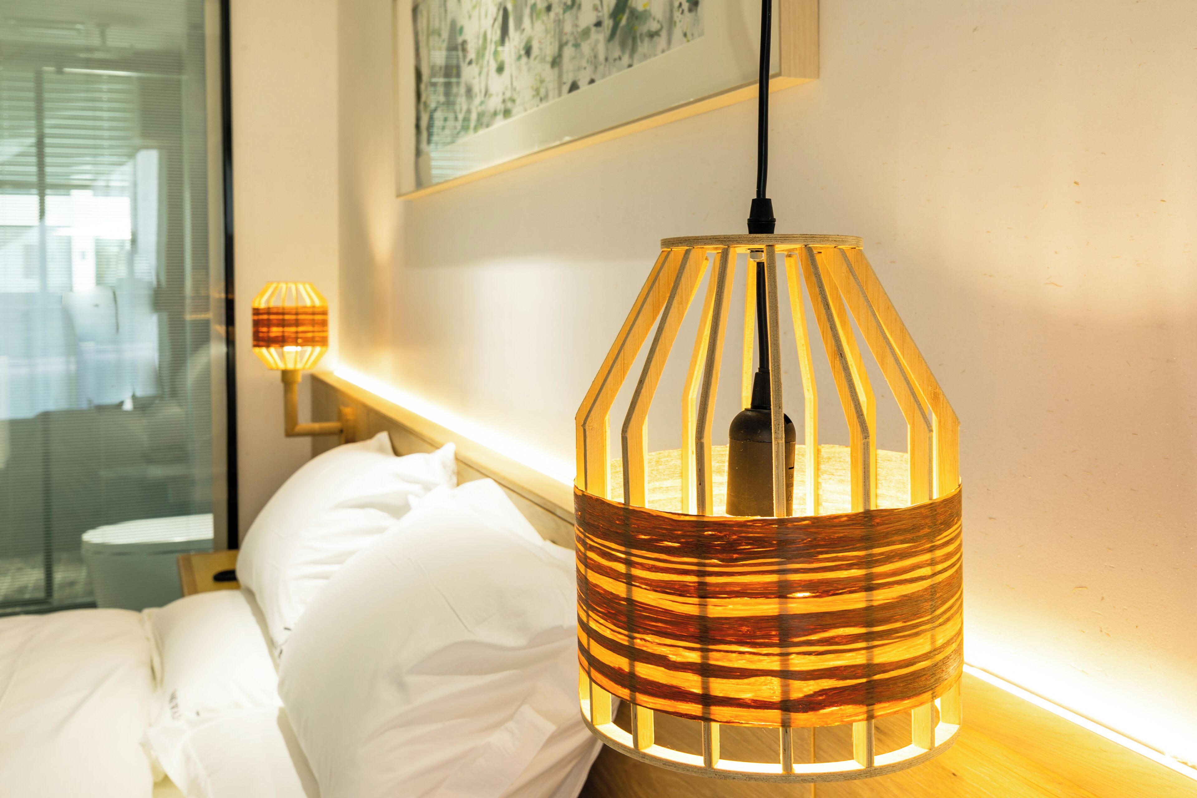 Uma cama com lençóis brancos, um abajur e um quadro pendurado na parede.