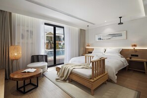 Quarto de hotel moderno com cama, mesas de cabeceira, uma cadeira, uma mesinha e vista para uma piscina e edifícios.
