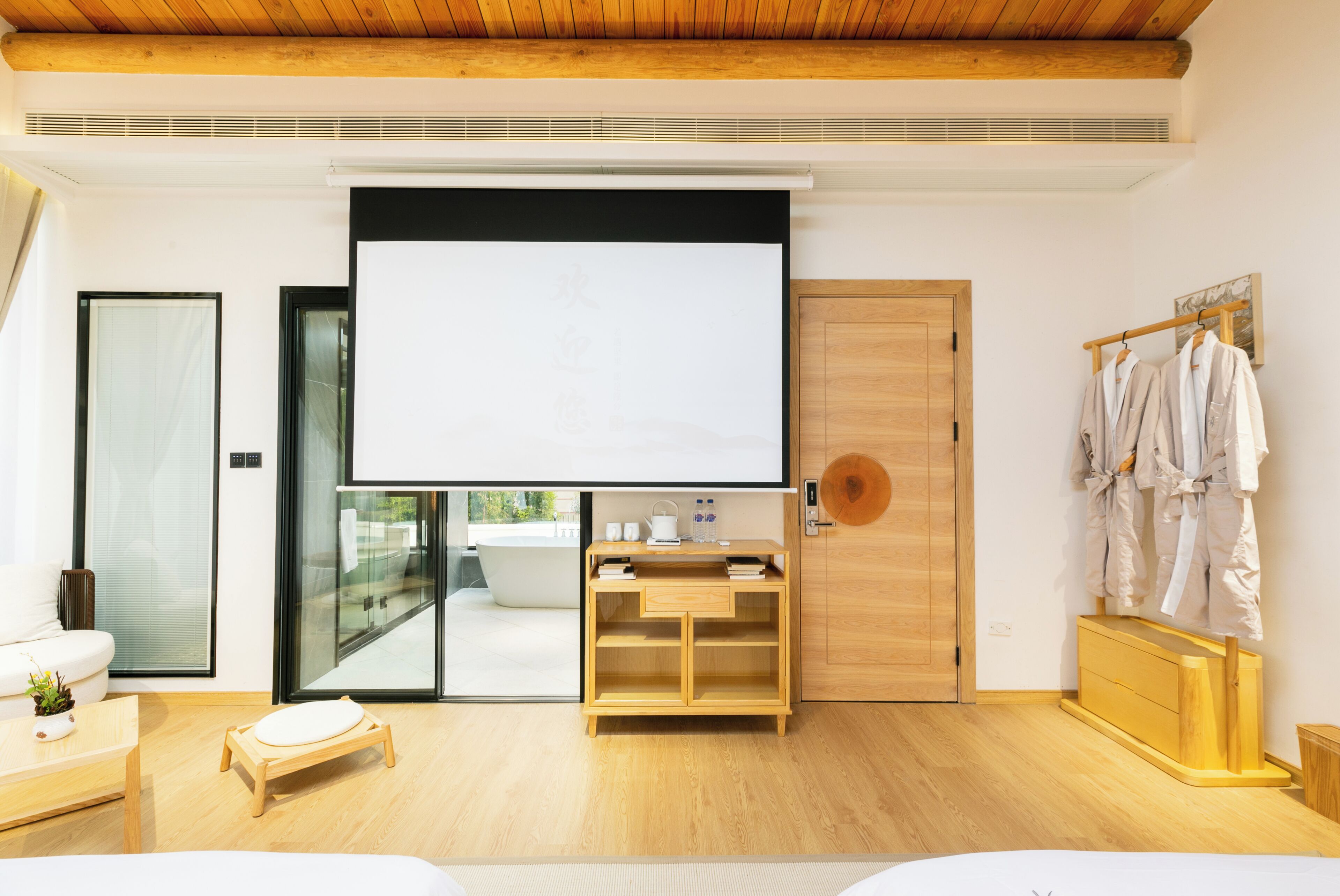 Quarto moderno com tela grande, móveis de madeira, banheira e um cabideiro.