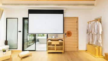 Quarto moderno com tela grande, móveis de madeira, banheira e um cabideiro.