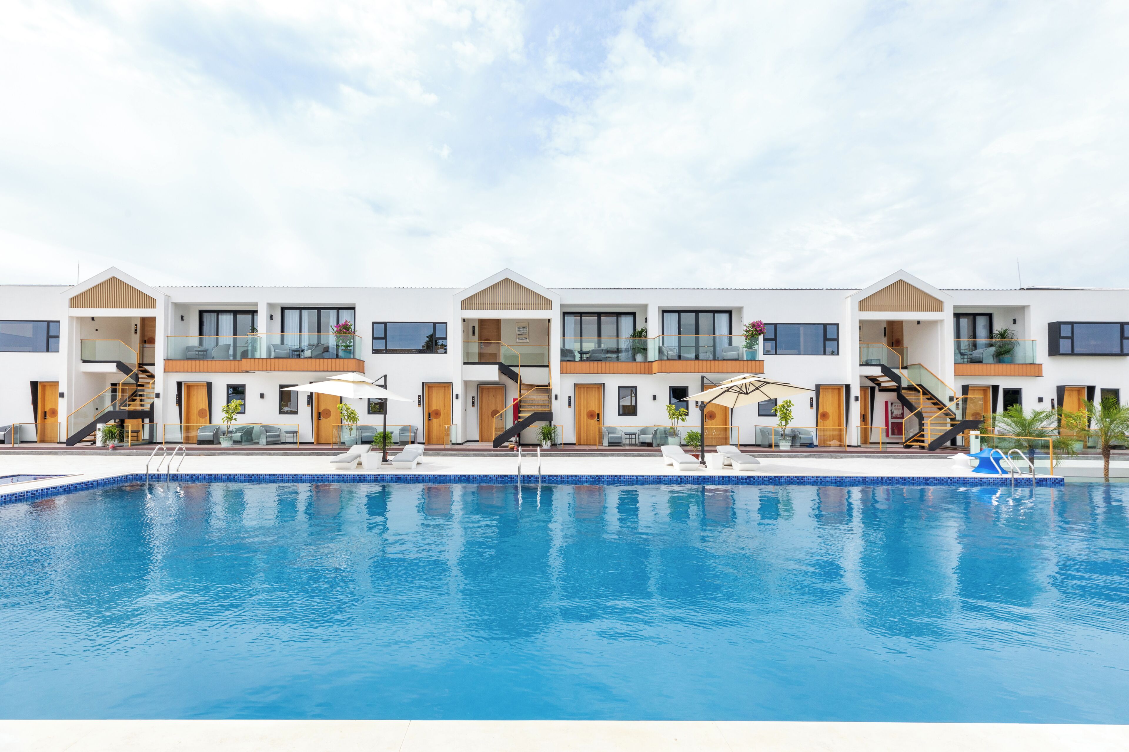 Um hotel moderno com piscina, várias varandas e céu limpo.