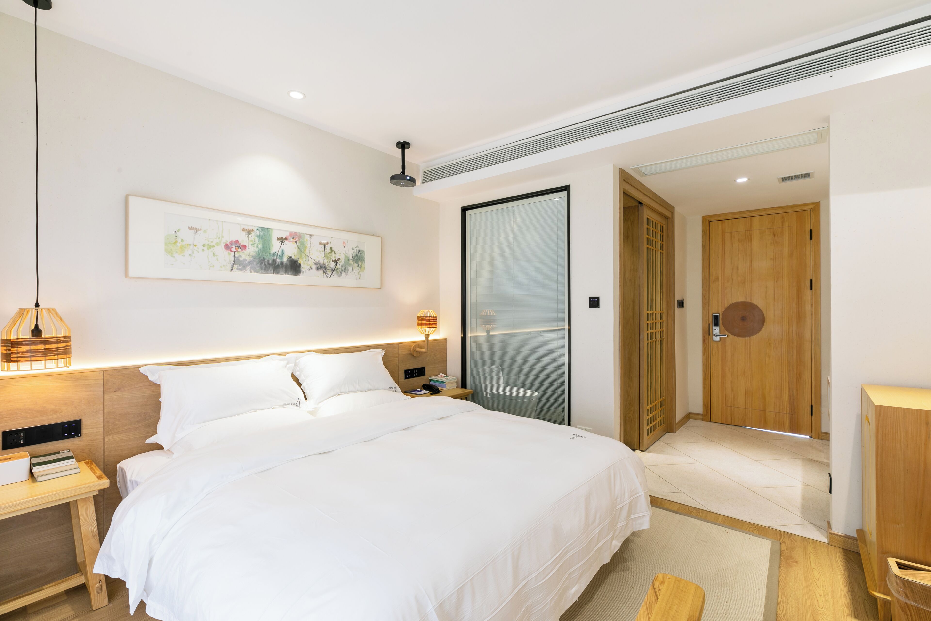 Quarto de hotel com uma cama grande, mesas de cabeceira, uma obra de arte na parede, uma porta de vidro deslizante e uma porta de madeira.