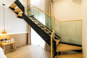 Interior moderno com escada, soalho de madeira, mesa de cabeceira com abajur e janela com cortinas.