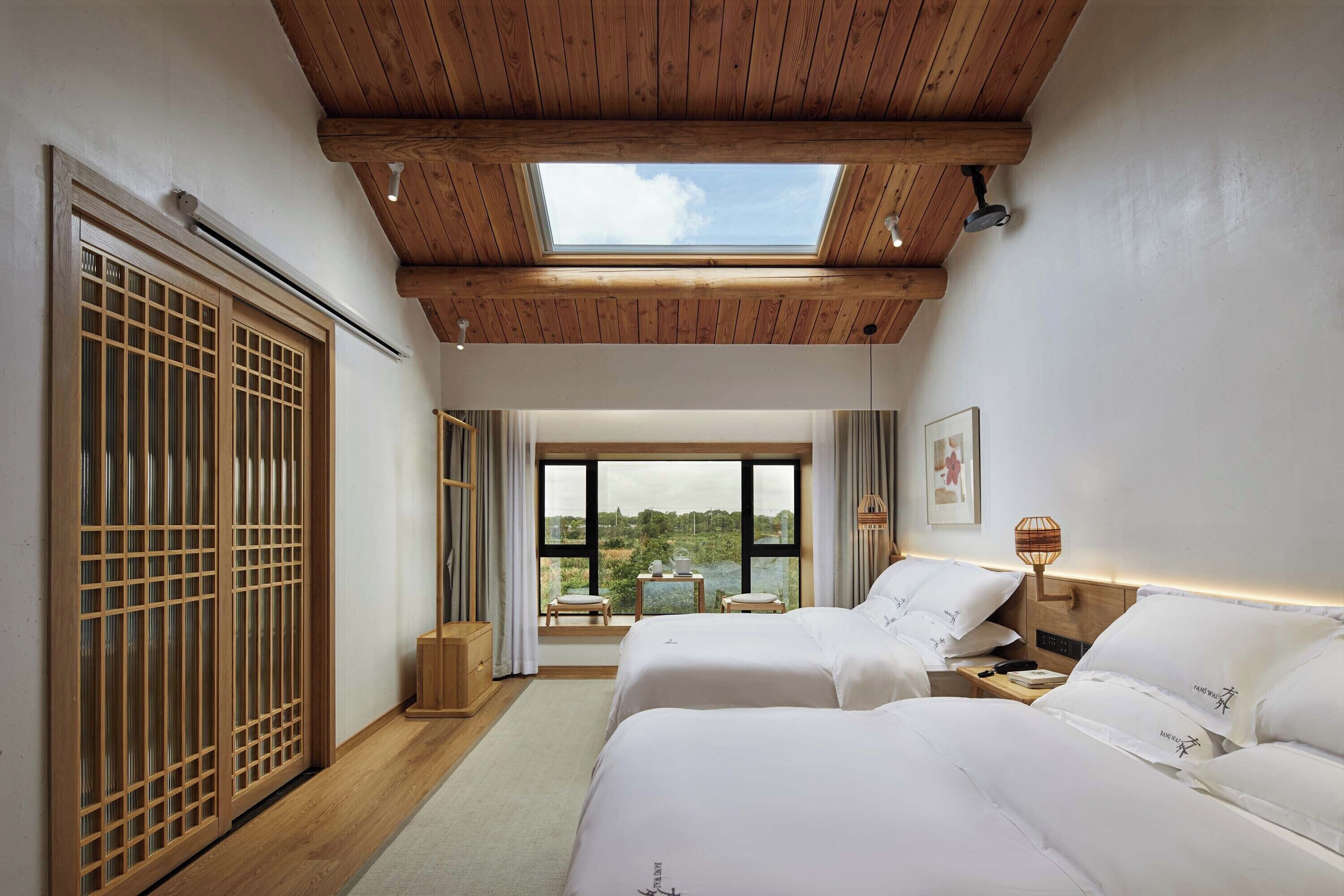 Quarto de hotel com claraboia, duas camas, vista para o verde e decoração tradicional.