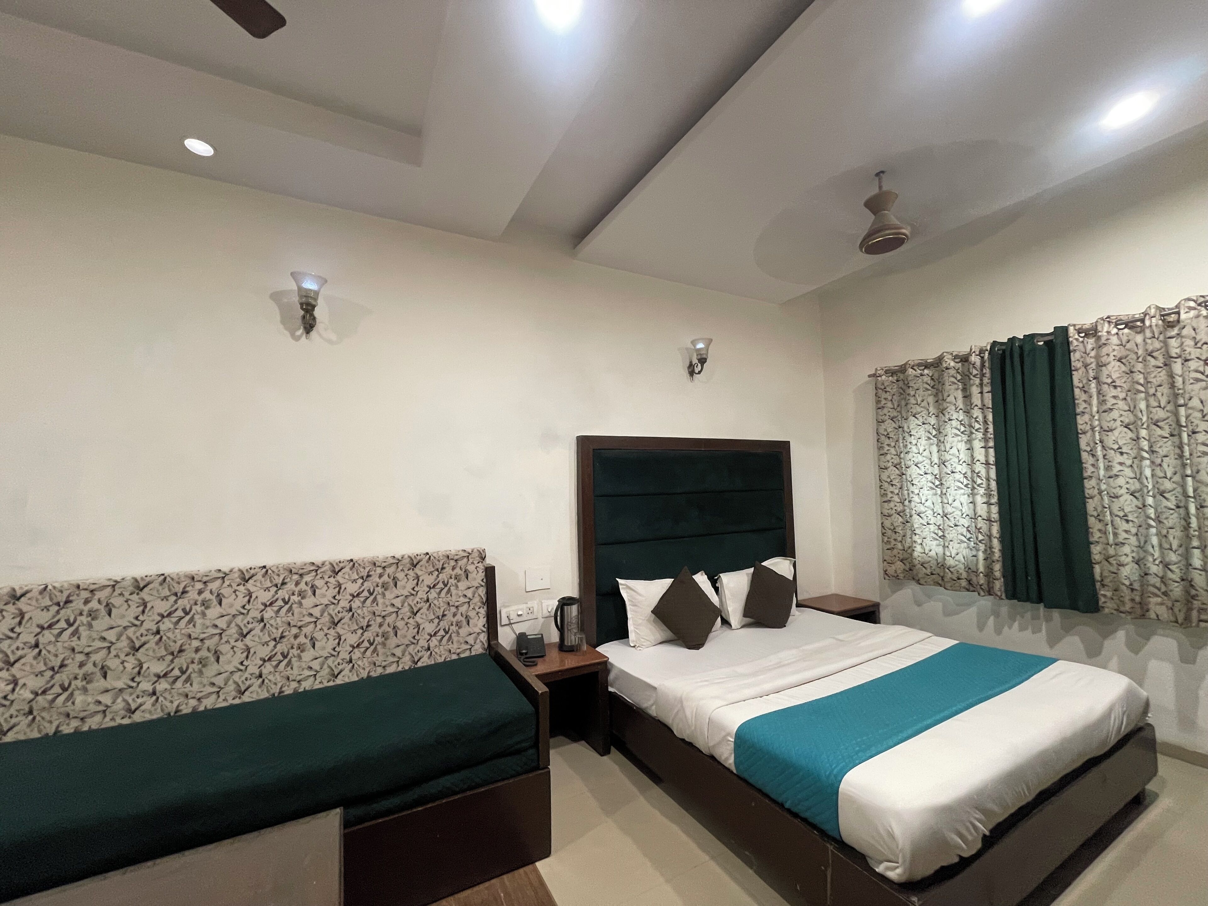 Quarto de hotel com cama, mesa de cabeceira, luminária na parede e ventilador de teto.