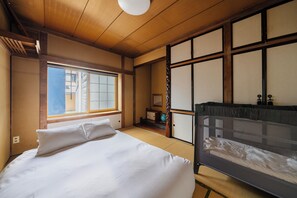 Quarto japonês tradicional com chão de tatame, cama com roupa de cama branca, porta de tela deslizante shoji e vista para o exterior.