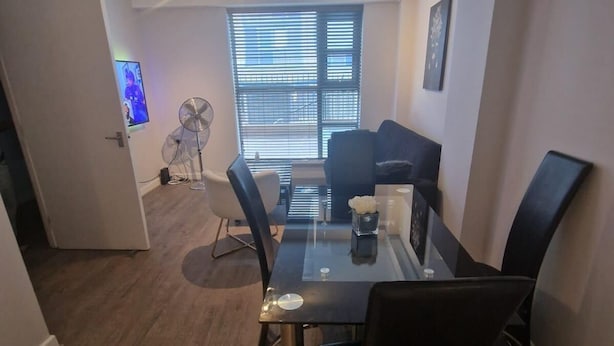 Uma sala de jantar com mesa, cadeiras, um ventilador e uma janela com persianas.