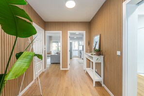 Um corredor com painéis de madeira, um console branco com uma planta e uma porta que dá para um quarto.