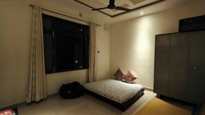 Quarto com cama, guarda-roupa, janela com cortinas e ventoinha no teto.